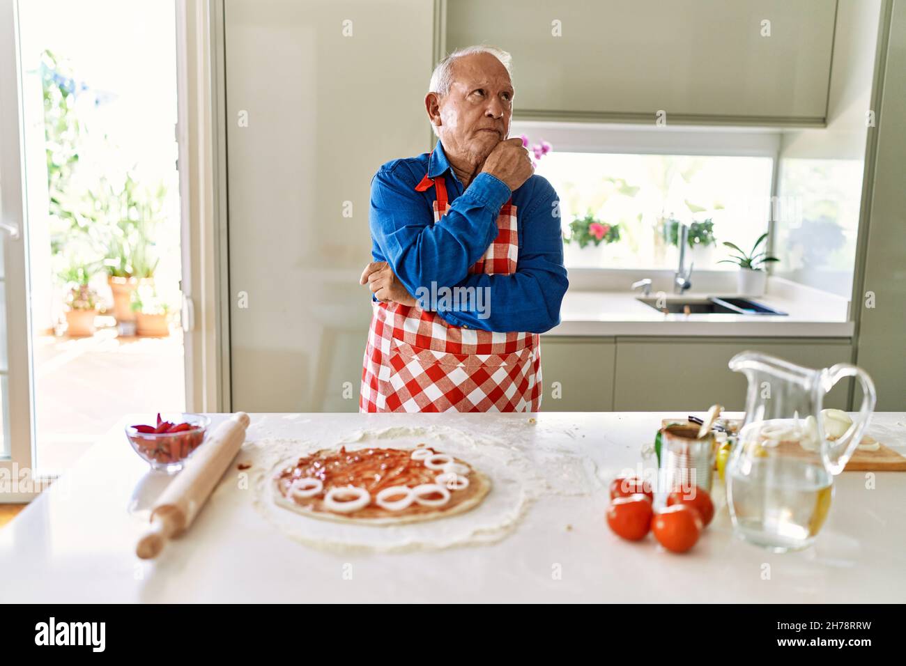Senior man with grey hair cooking pizza at home kitchen serious face ...