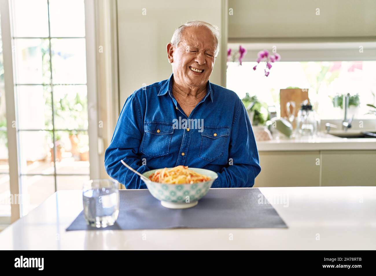 Senior man with grey hair eating pasta spaghetti at home with hand on ...