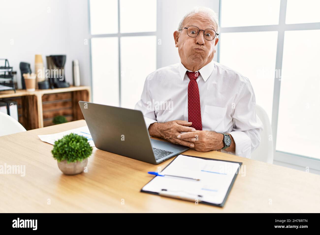 Senior man working at the office using computer laptop puffing cheeks ...
