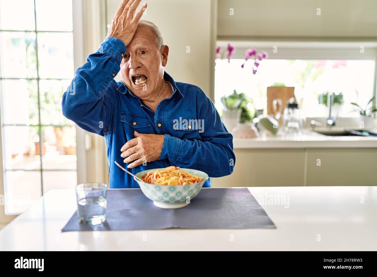 Senior man with grey hair eating pasta spaghetti at home surprised with ...