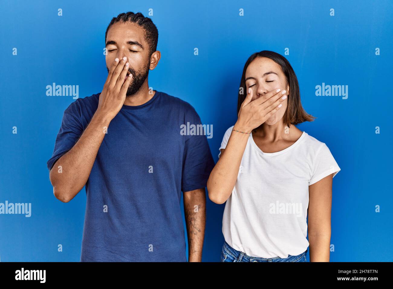Young hispanic couple standing together bored yawning tired covering ...