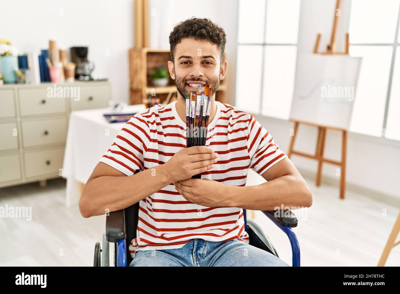 Young arab disabled artist man holding paintbrushes sitting on ...