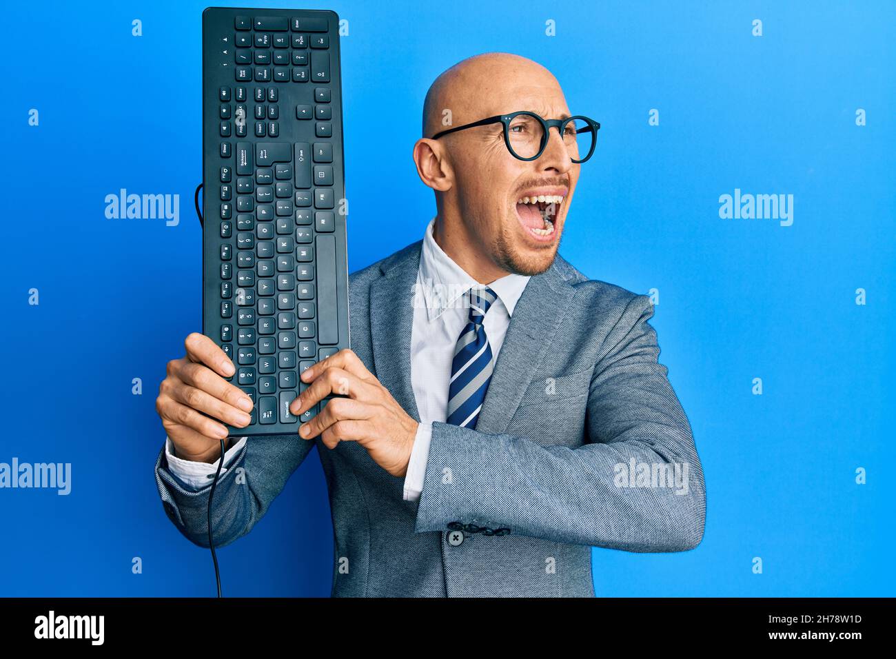 Bald man with beard holding keyboard angry and mad screaming frustrated ...