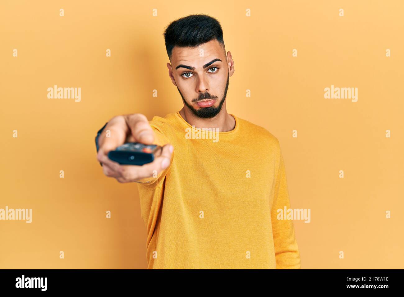 Young hispanic man with beard holding television remote control ...