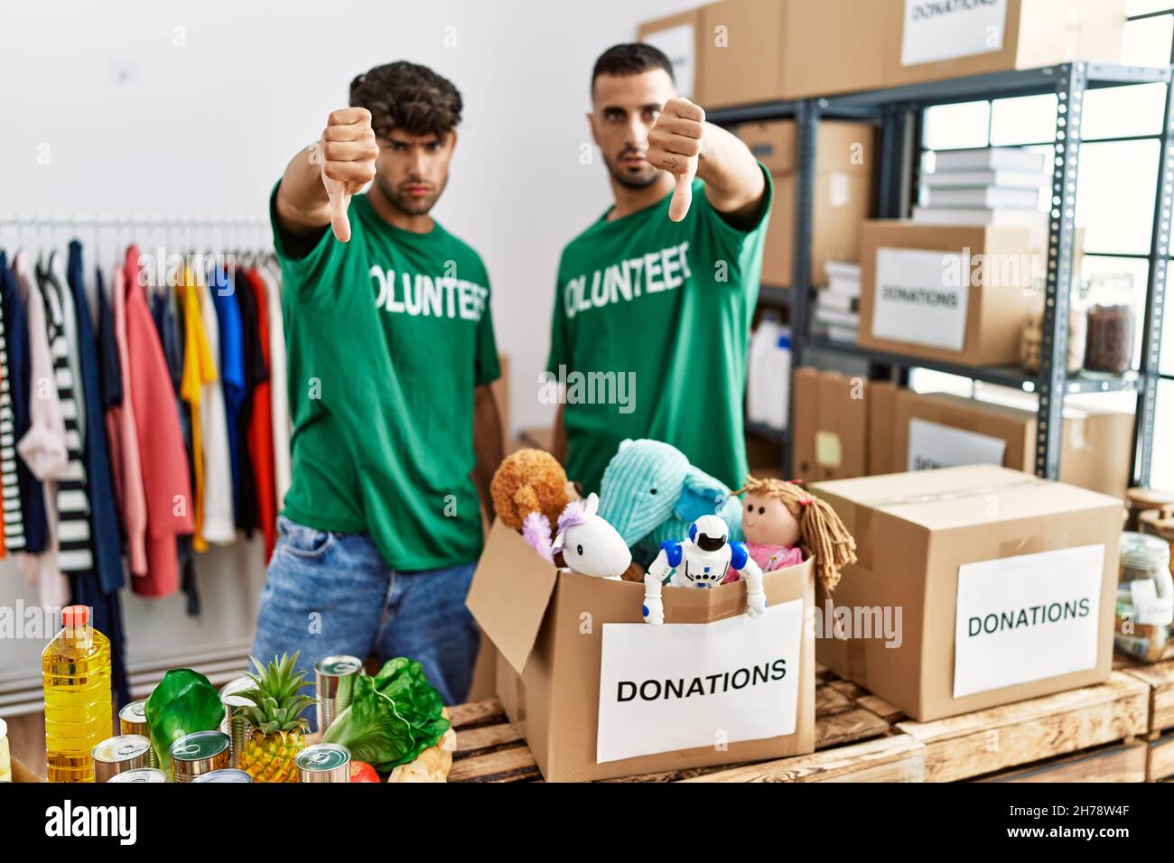 Young gay couple wearing volunteer t shirt at donations stand looking ...