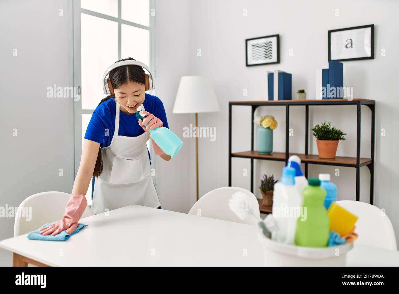 Young chinese housewife cleaning and singing using sprayer at home ...