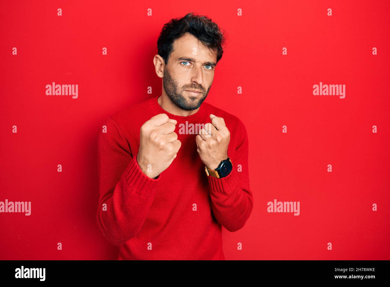 Handsome man with beard wearing casual red sweater ready to fight with ...