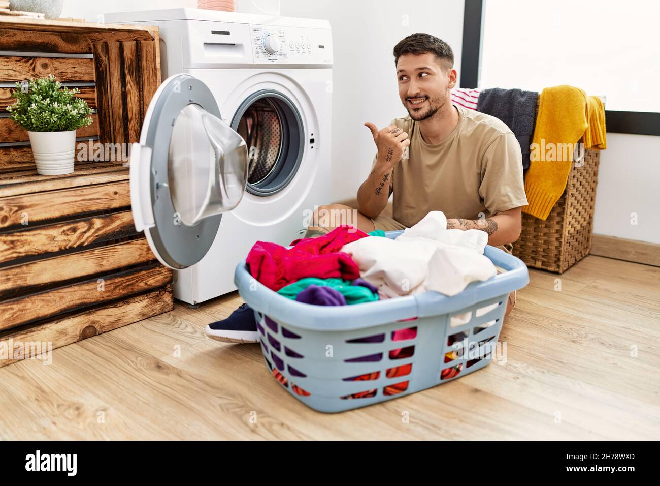 Young handsome man putting dirty laundry into washing machine smiling ...