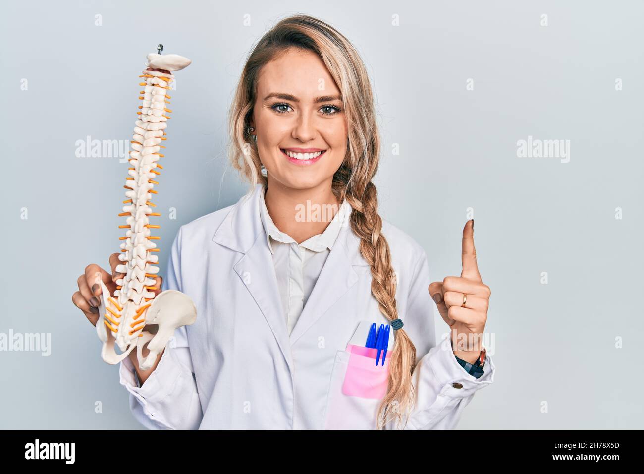 Beautiful young blonde doctor woman holding anatomical model of spinal ...