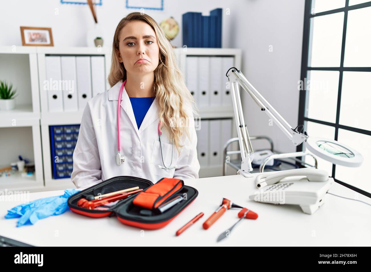 Young beautiful doctor woman with reflex hammer and medical instruments ...