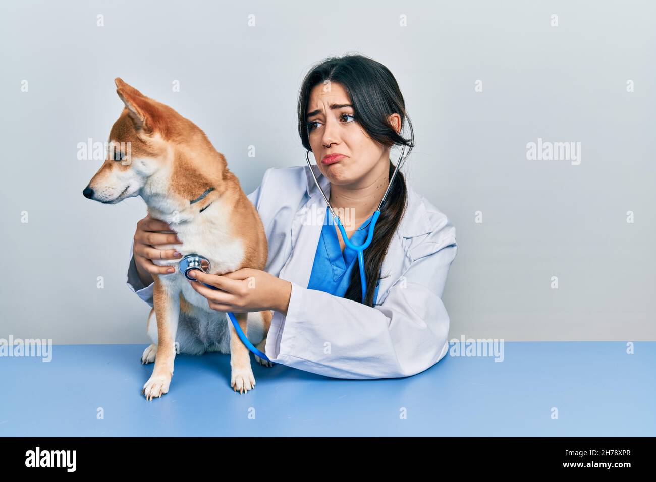 Beautiful hispanic veterinarian woman checking dog health depressed and ...