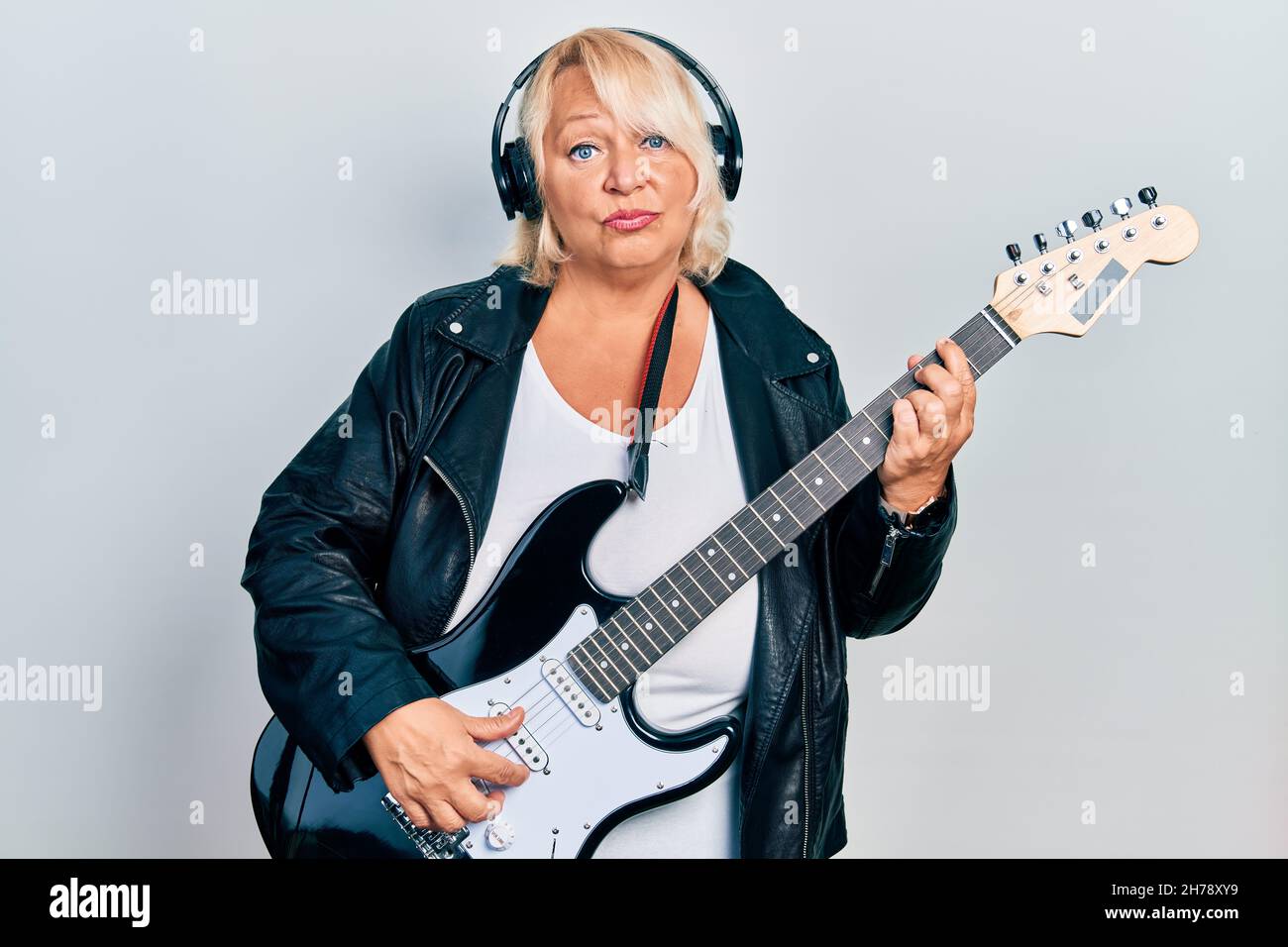Middle age blonde woman playing electric guitar using headphones ...