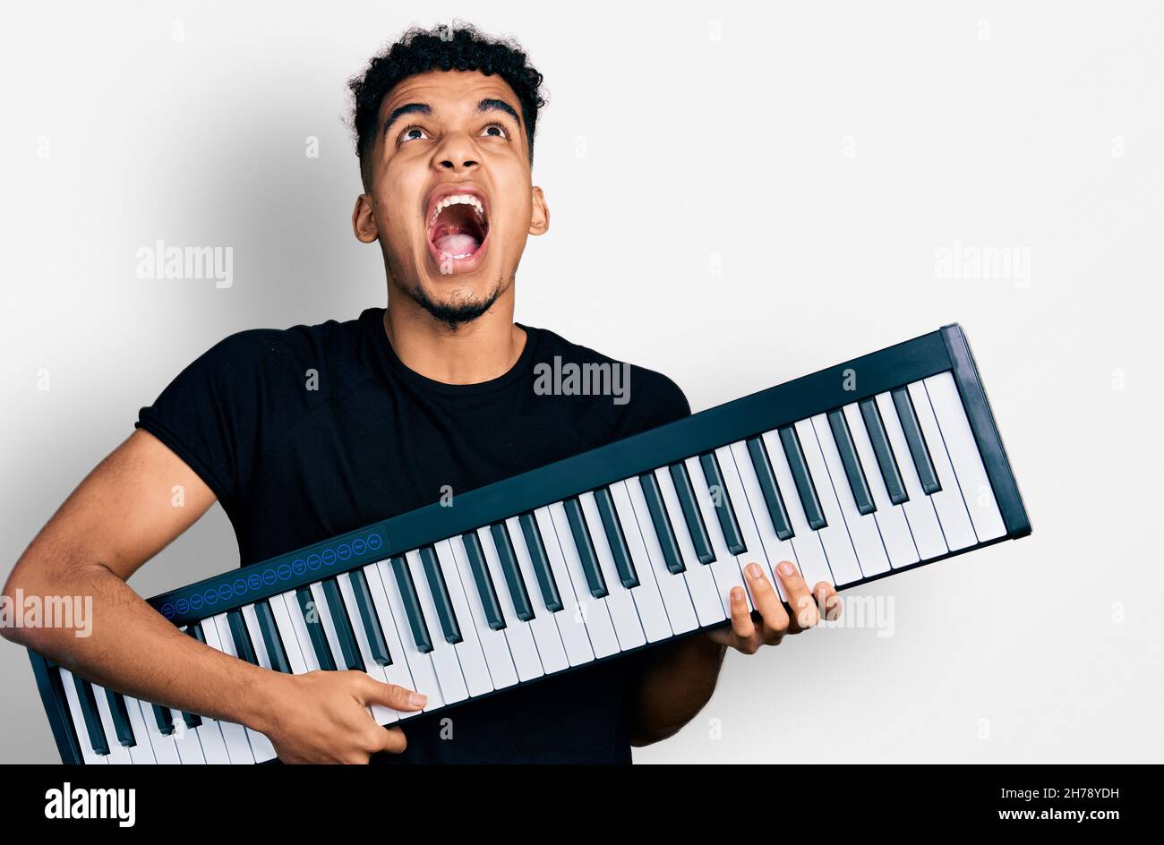 Young african american man holding piano keyboard angry and mad ...