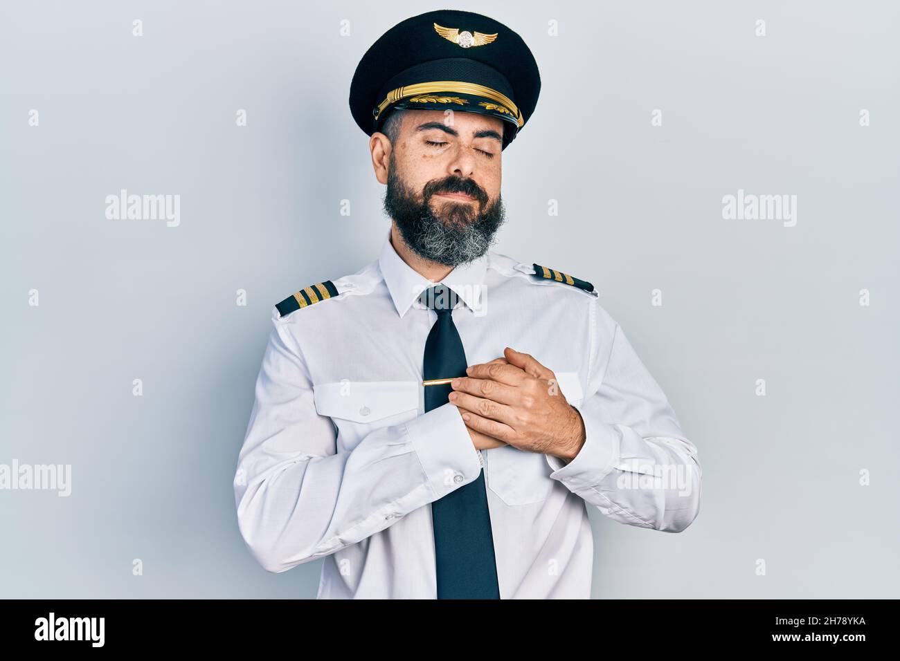 Young hispanic man wearing airplane pilot uniform smiling with hands on ...