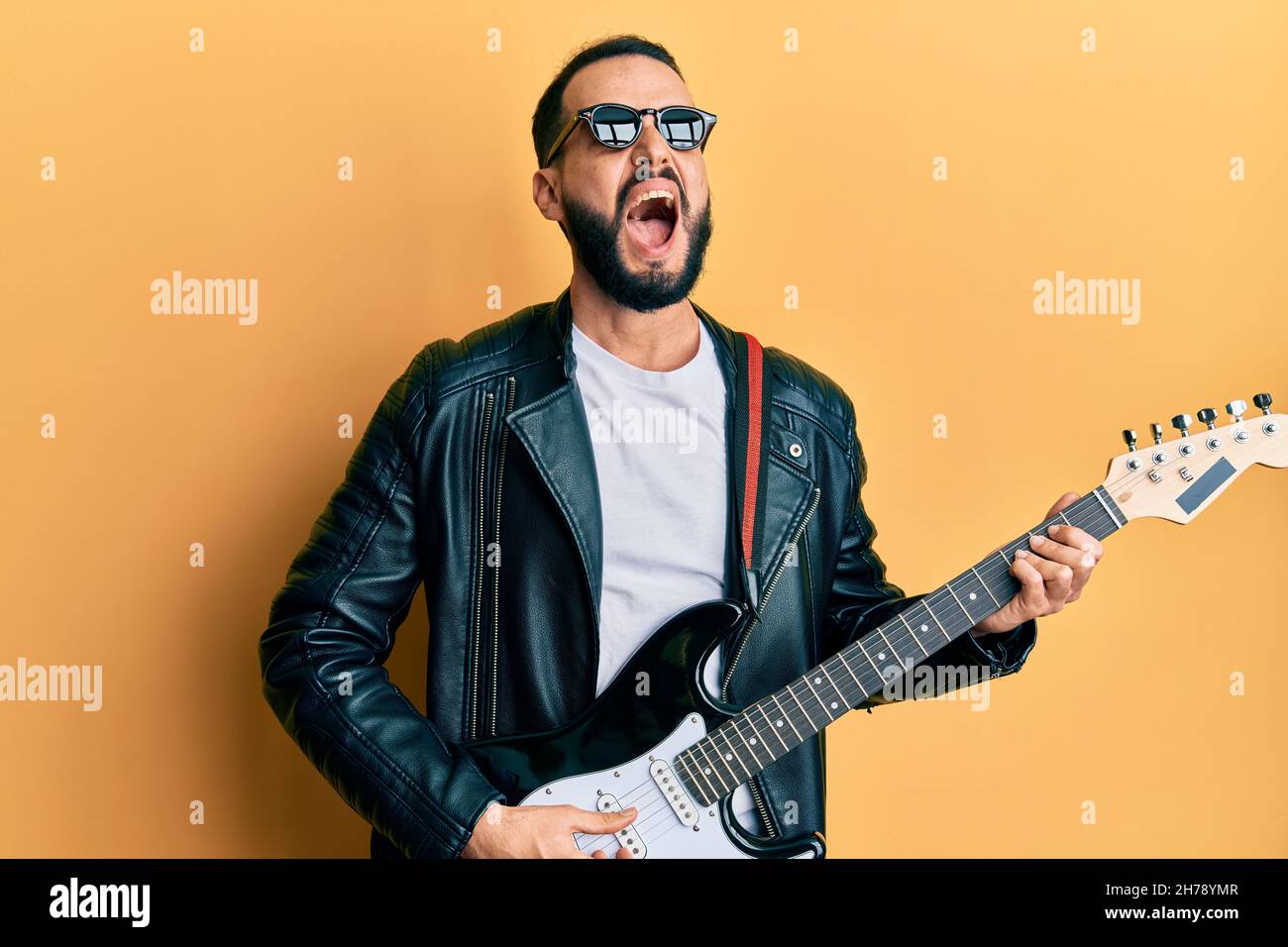 Young man with beard playing electric guitar angry and mad screaming ...