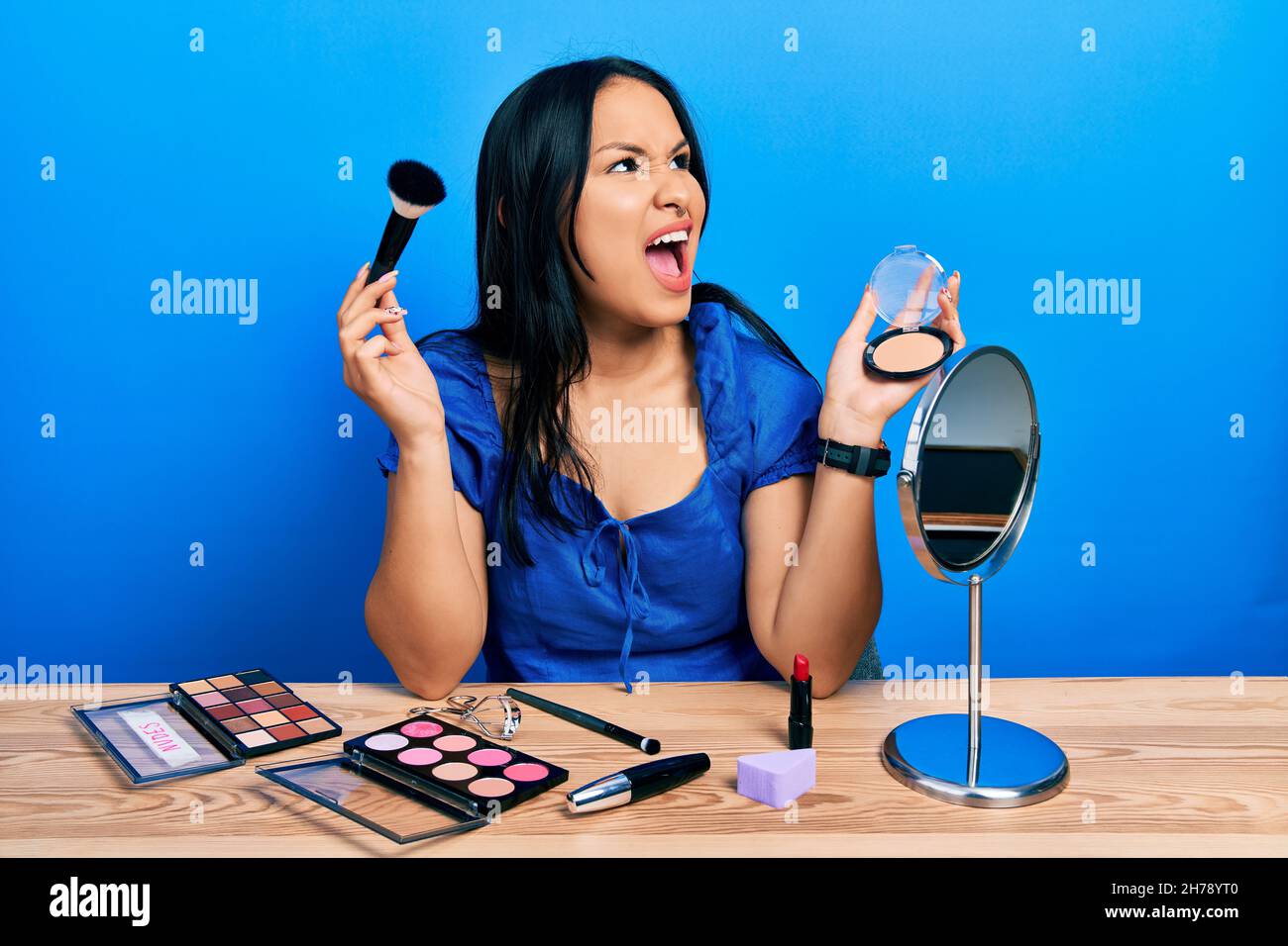 Beautiful hispanic woman with nose piercing holding makeup powder and ...