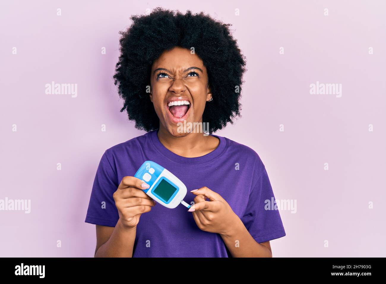 Young african american woman holding glucometer device angry and mad ...
