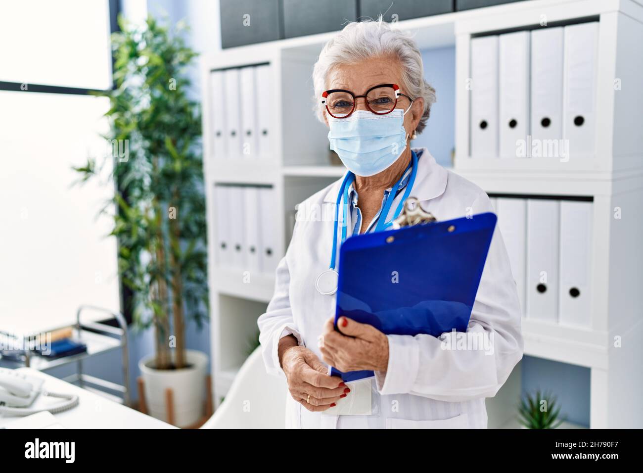 Senior woman with grey hair wearing doctor uniform and safety mask ...