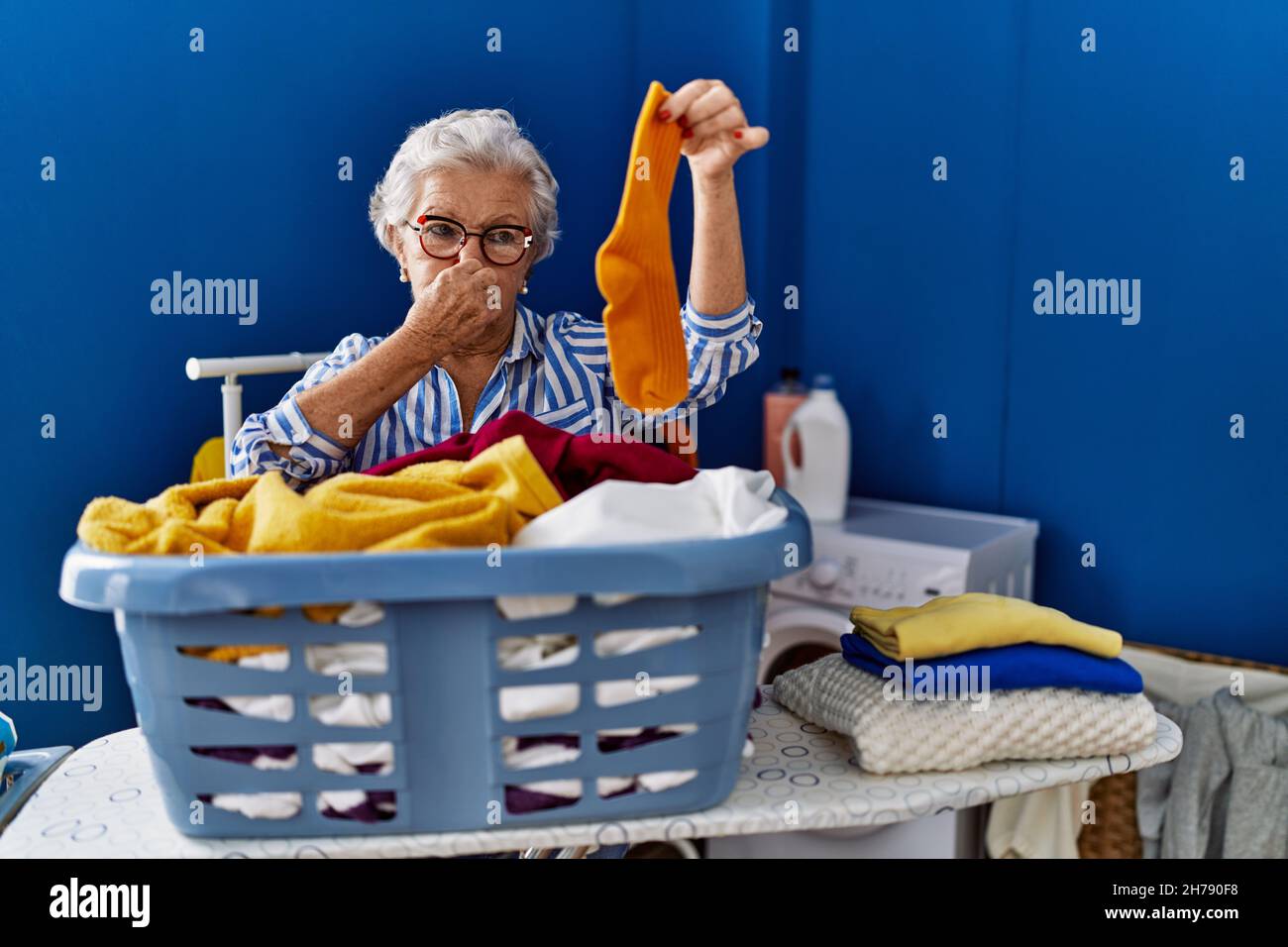 Senior grey-haired woman smelling odor of dirty sock at laundry room ...