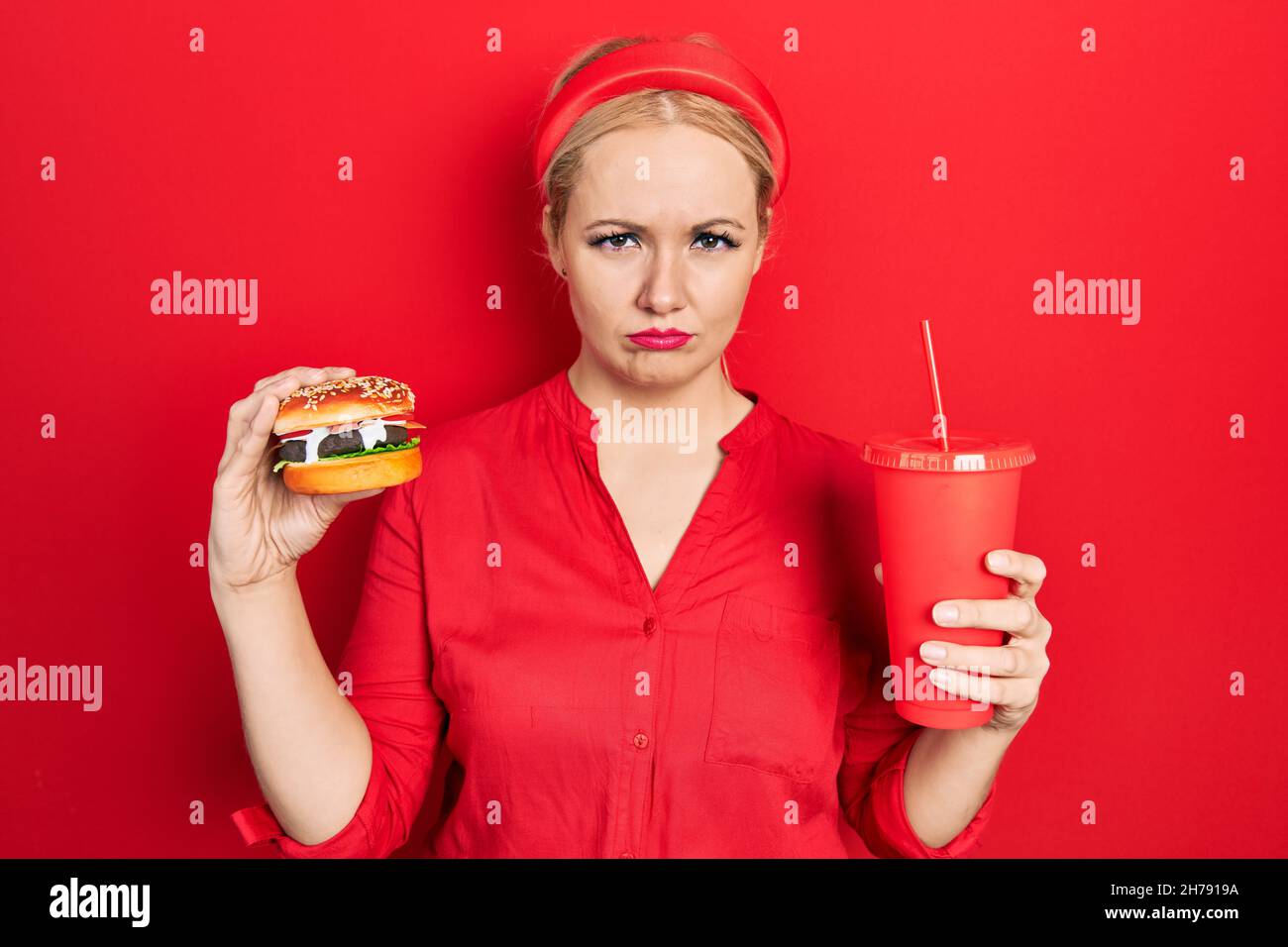 Young blonde woman eating a tasty classic burger with fries and soda ...