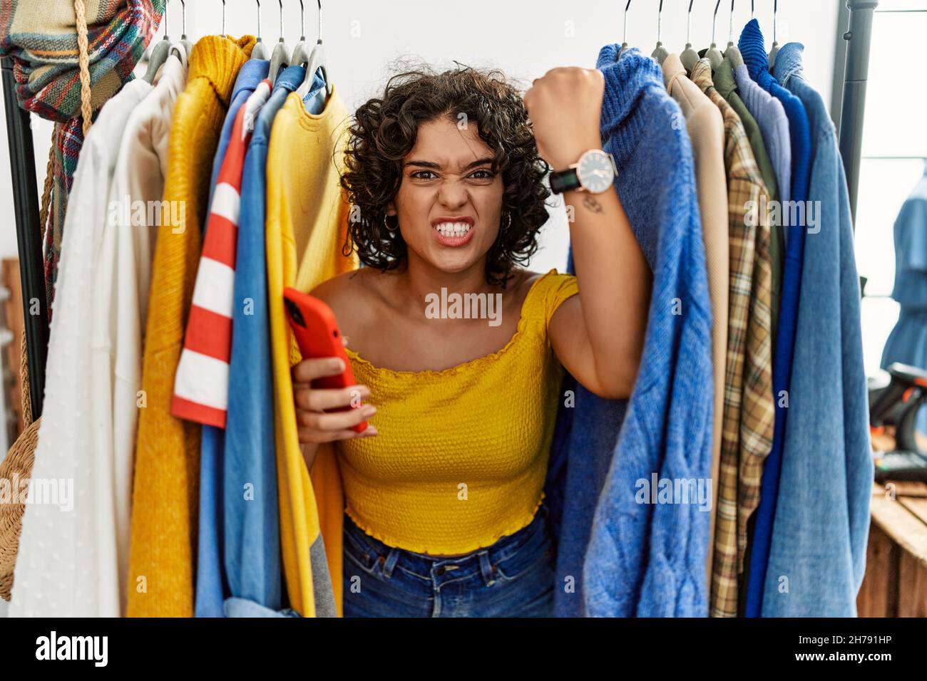 Young hispanic woman searching clothes on clothing rack using ...