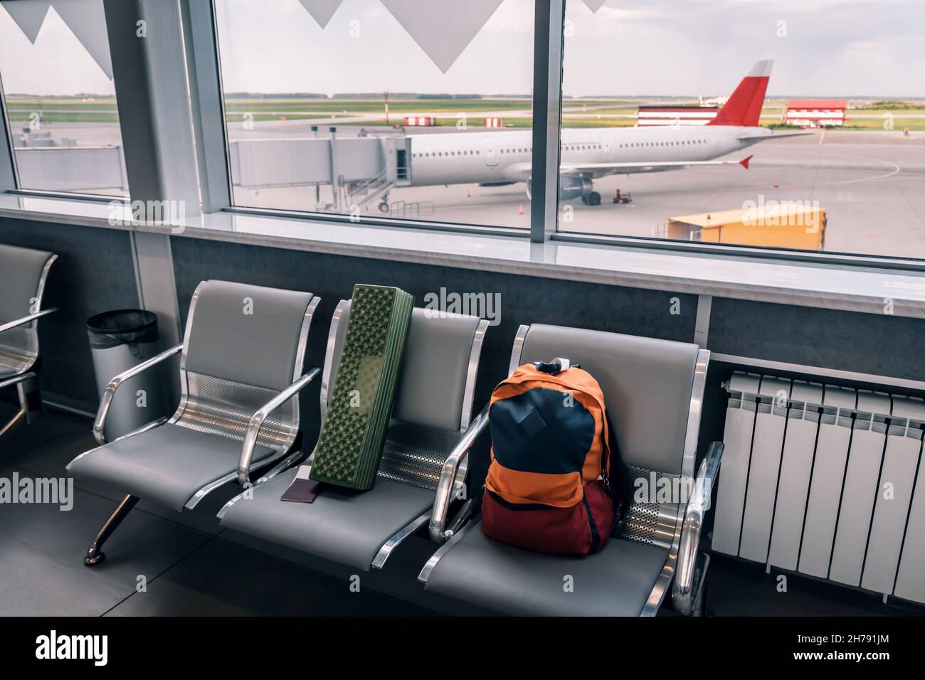 A small backpack is hand luggage on a bench with a view of the gate and ...