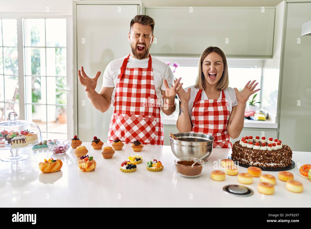 Young couple cooking pastries at the kitchen celebrating mad and crazy ...