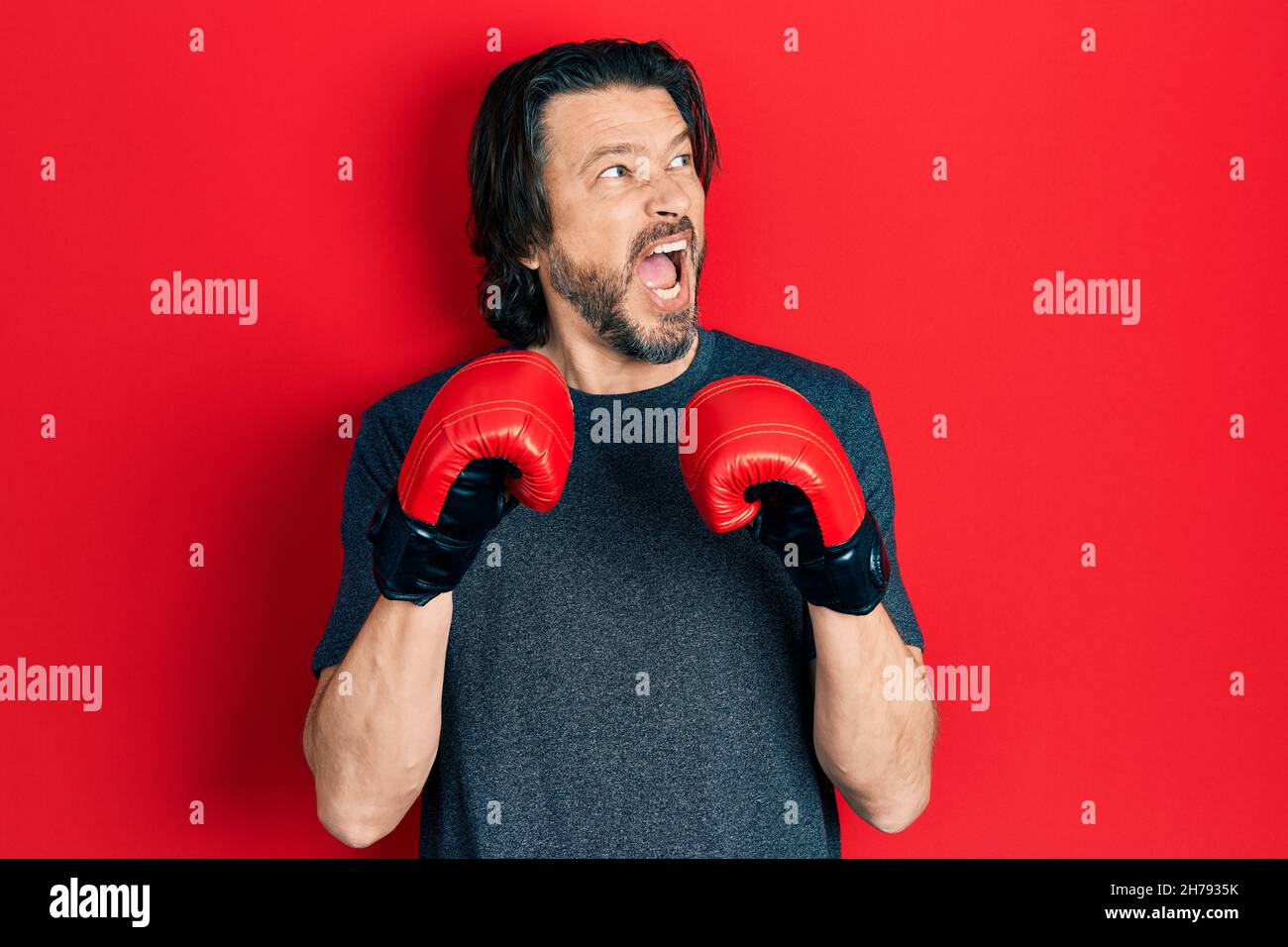 Middle age caucasian man using boxing gloves angry and mad screaming ...