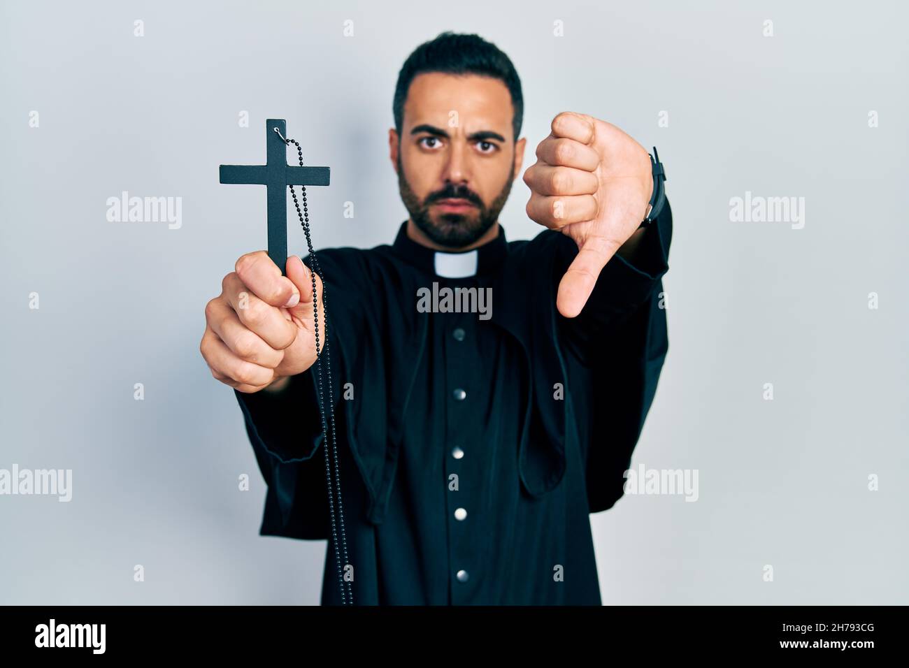 Handsome hispanic priest man with beard holding catholic cross with ...