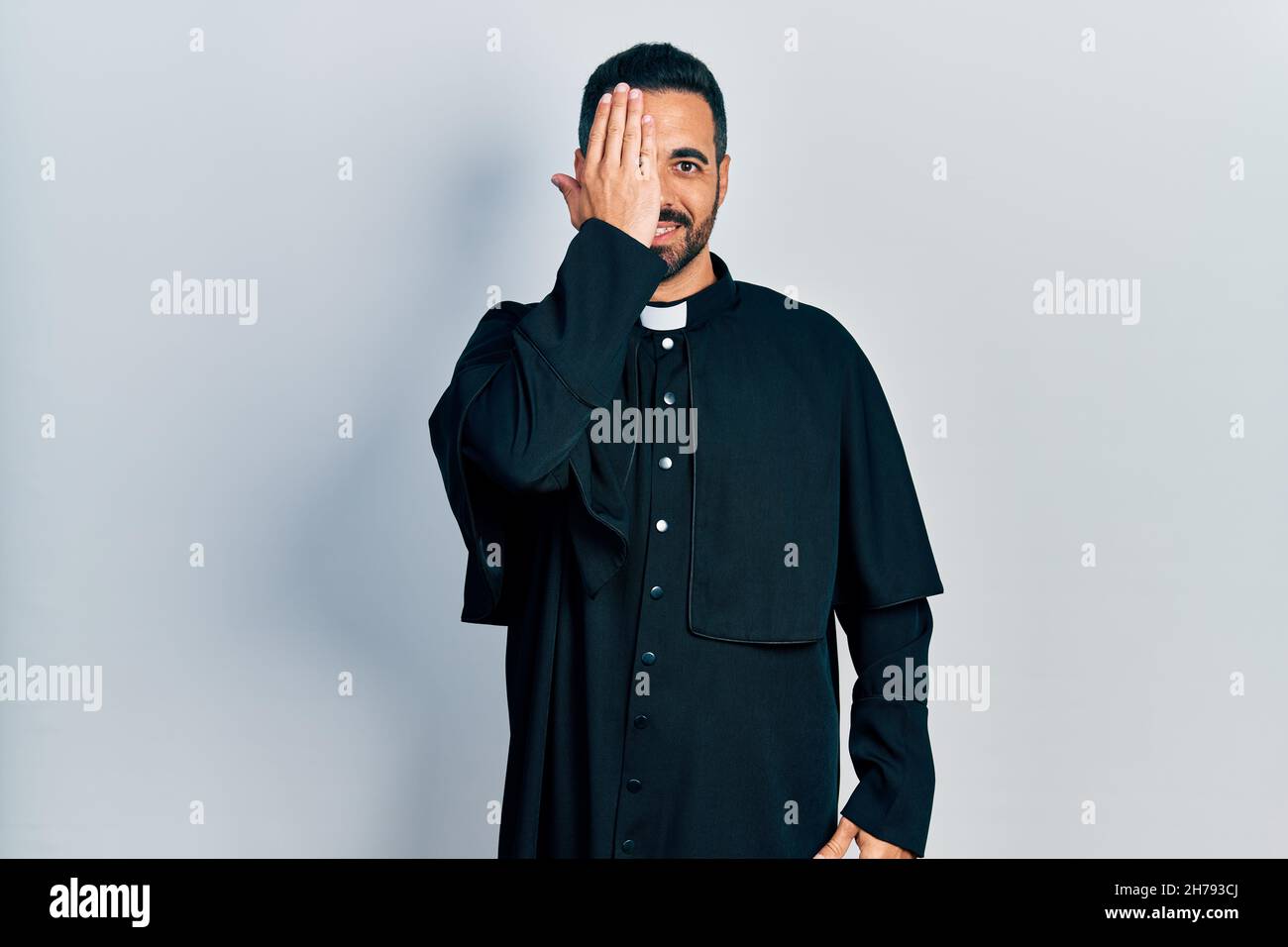 Handsome hispanic man with beard wearing catholic priest robe covering ...