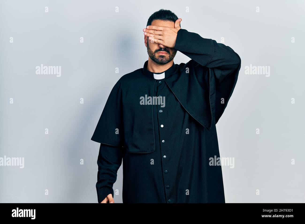 Handsome hispanic man with beard wearing catholic priest robe covering ...