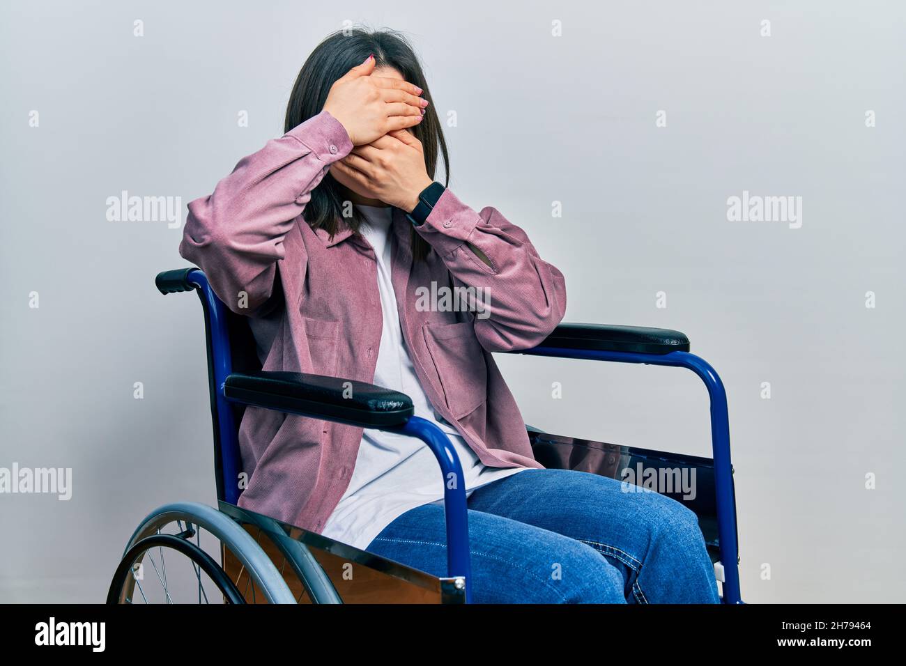 Young brunette woman sitting on wheelchair covering eyes and mouth with ...