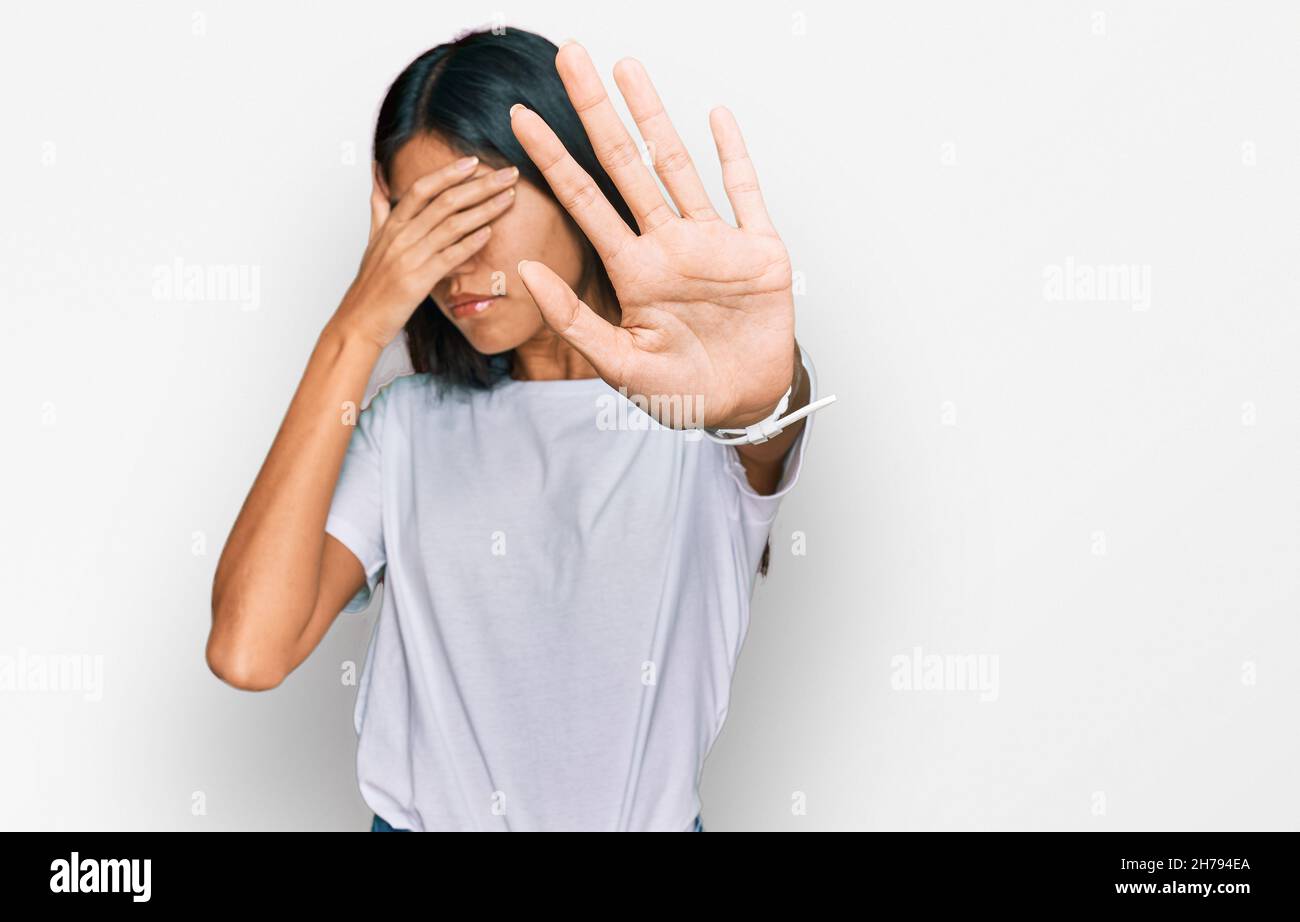Beautiful young asian woman wearing casual white t shirt covering eyes ...