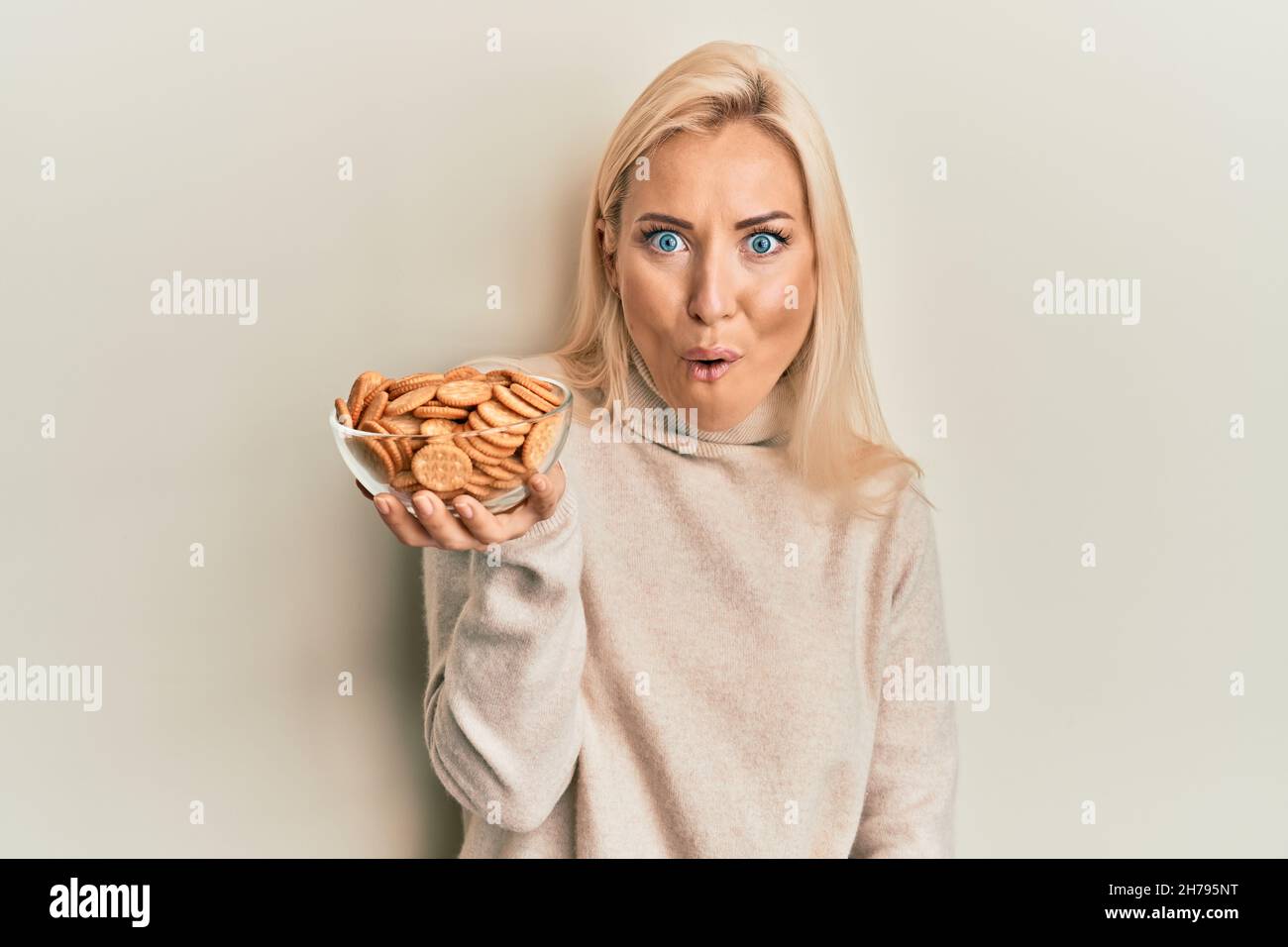 Young blonde woman cooking using baker whisk scared and amazed with ...