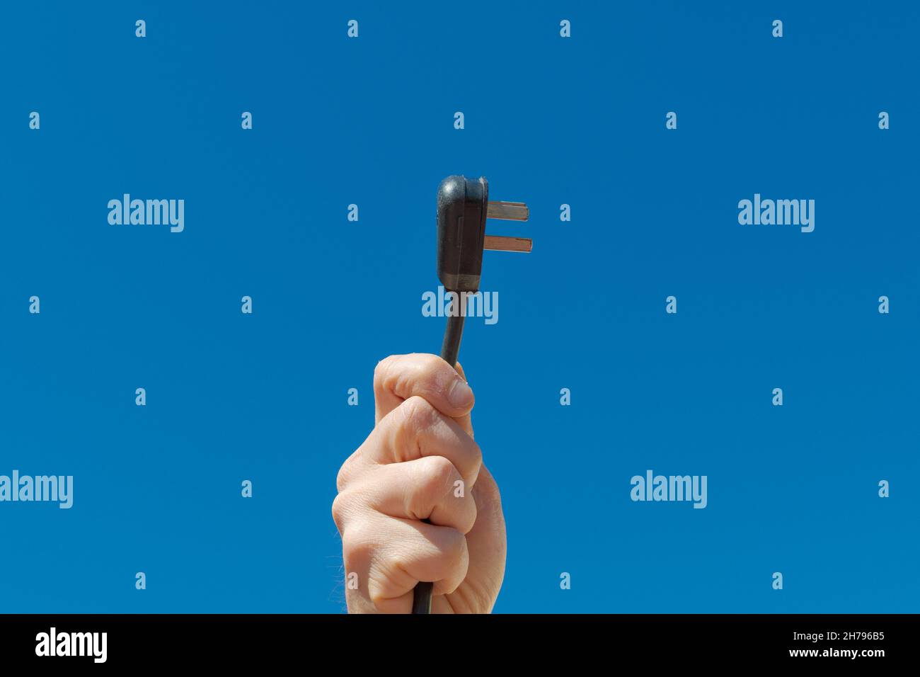 A low angle of a person holding a black plug under the blue sky Stock ...