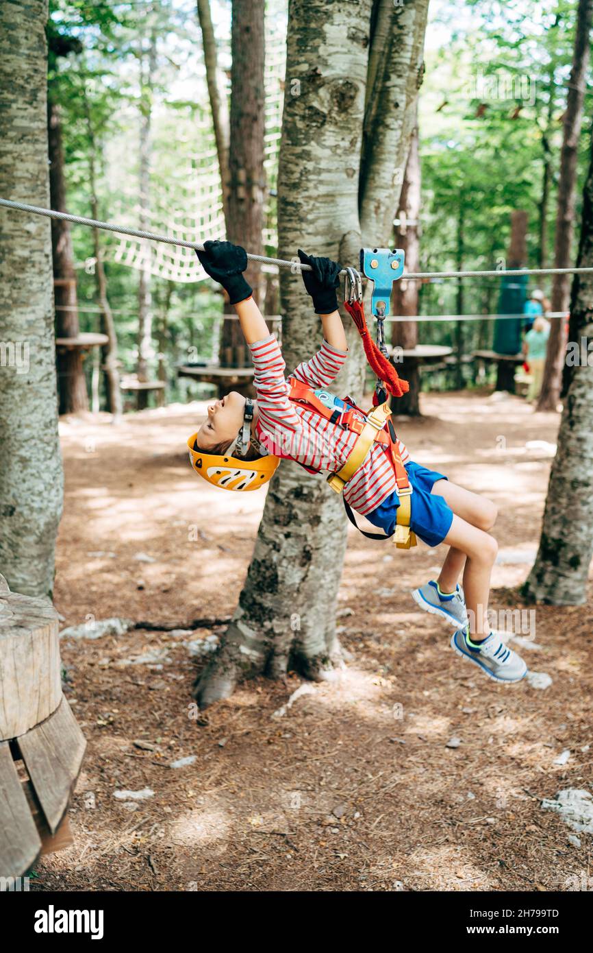 Boy climbs the zip line holding on to the safety rope with his hands ...