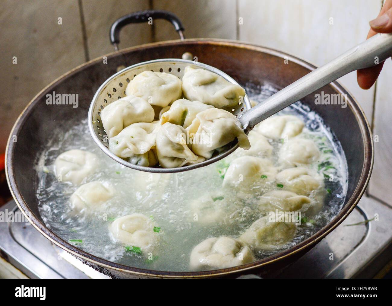 Chinese family cook dumplings and pick up the dumplings from the wok ...