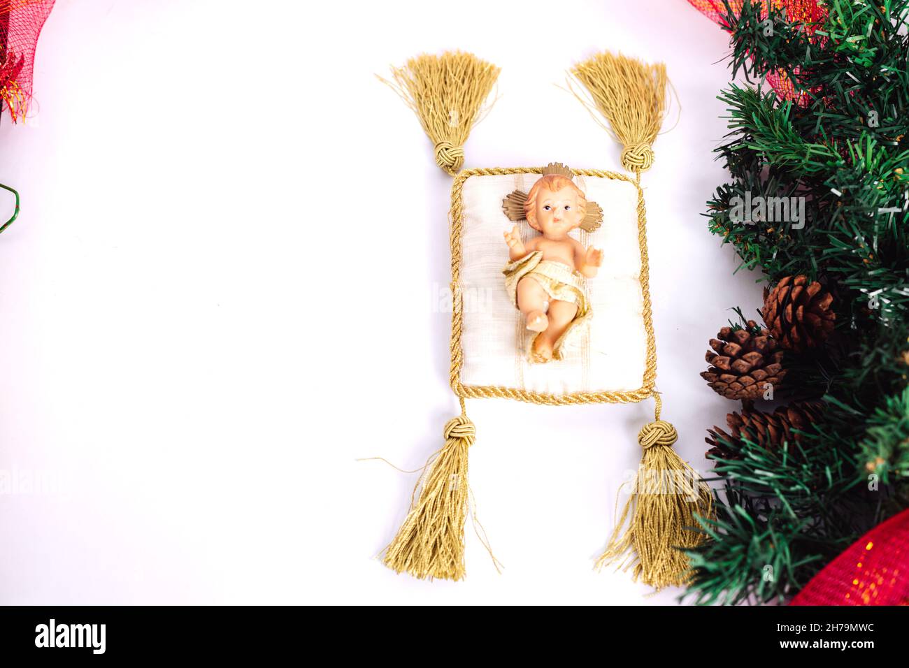 A statue of an infant Jesus with pine branches on a white background ...