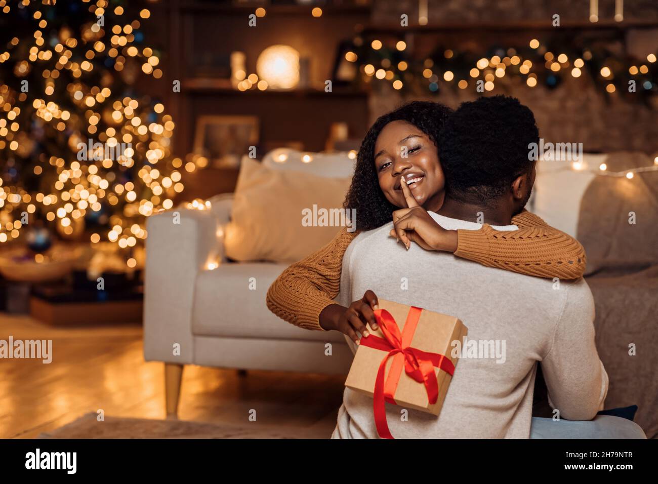 Young black woman hugging boyfriend, making silence gesture, holding ...