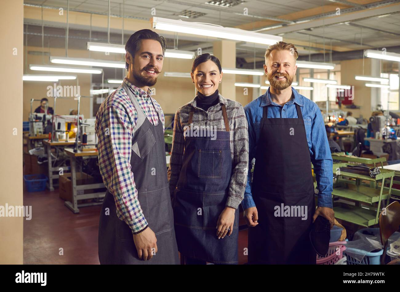 Portrait of three happy workers standing in a workshop at a shoe or ...