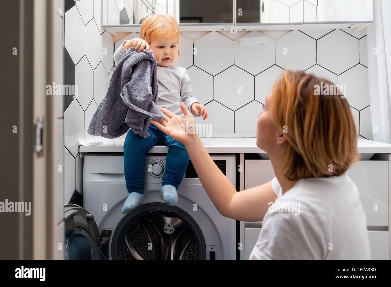 A mother and her little daughter loading laundry in the washing machine ...