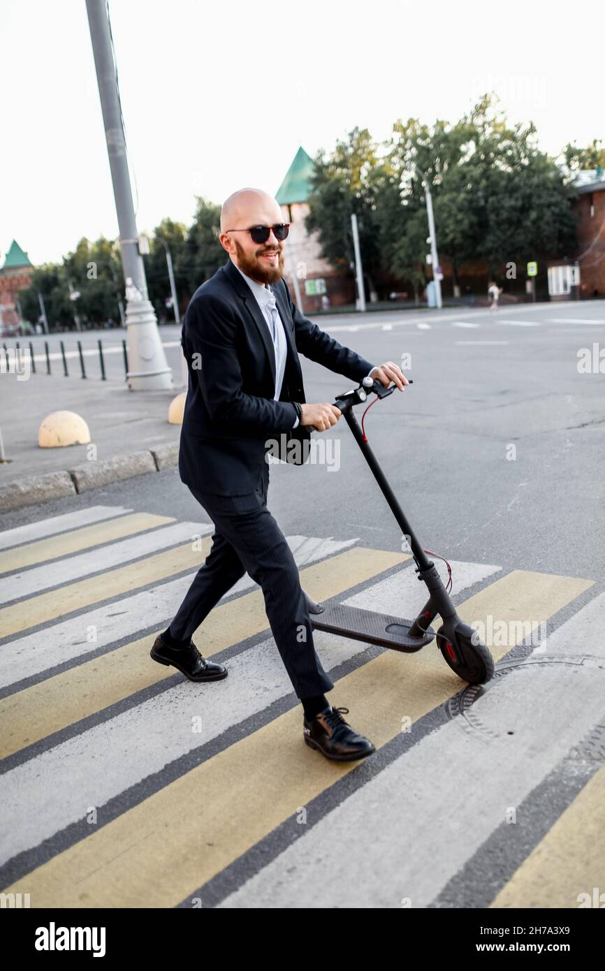Attractive business man riding a kick scooter at cityscape background ...