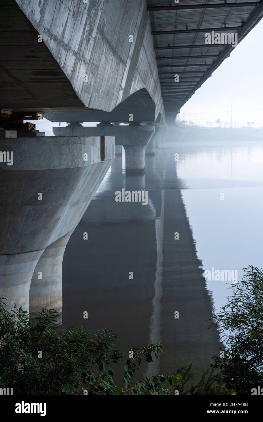 A vertical shot of the view under a bridge over a river with reflection ...