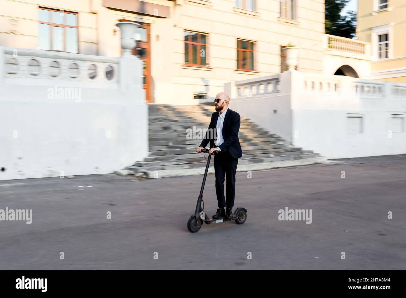 Attractive business man riding a kick scooter at cityscape background ...