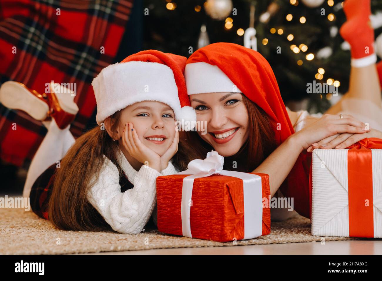 A happy little girl and her mom in Santa Claus hats are smiling with ...