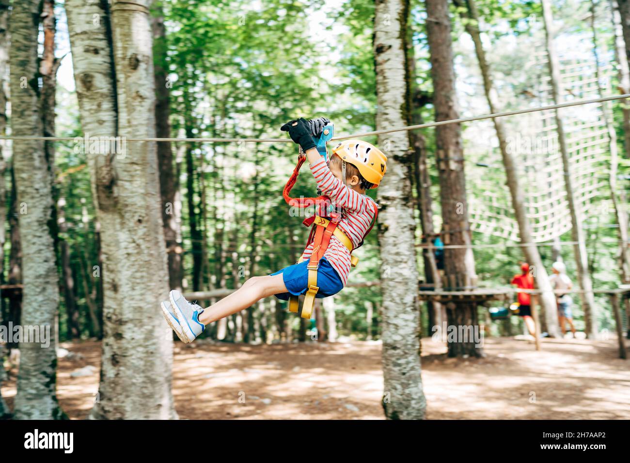 Boy riding a zip line holding on to the safety belt with his hands ...