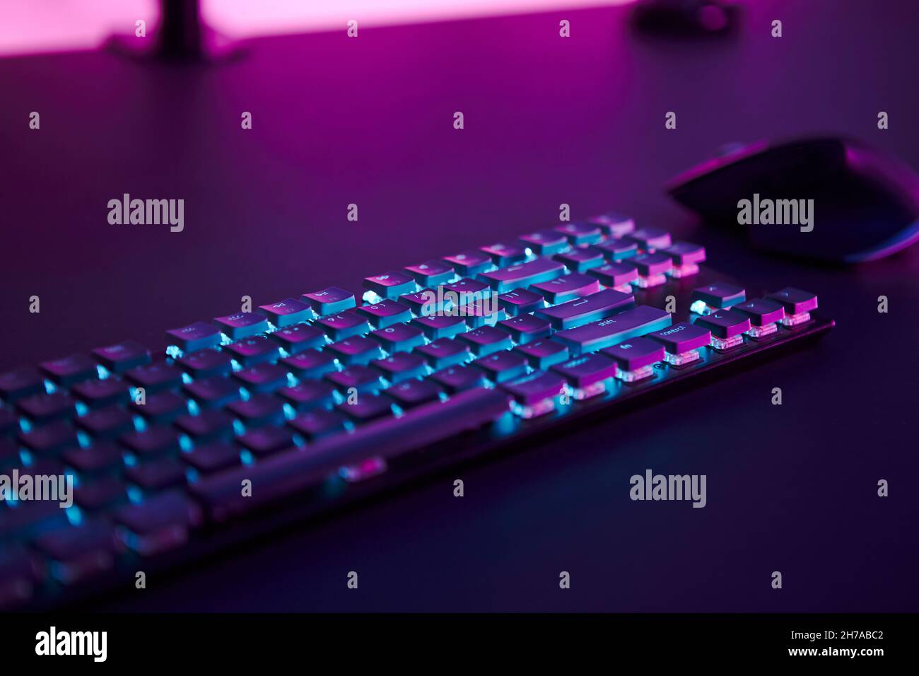 Computer mouse and illuminated keyboard laying on desk. Pink light in ...