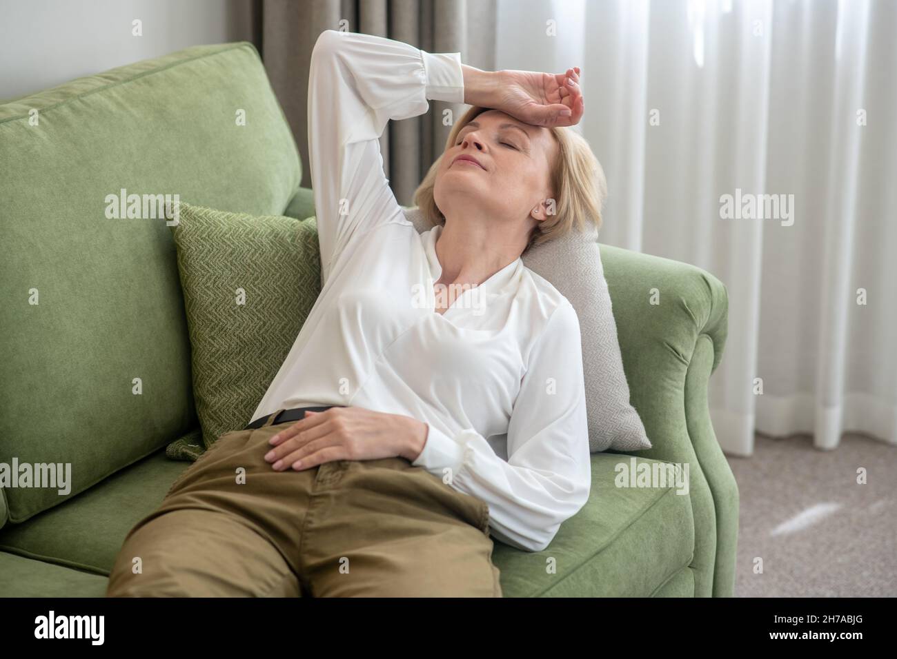 Blonde mid aged woman lying on the sofa and feeling bad Stock Photo - Alamy