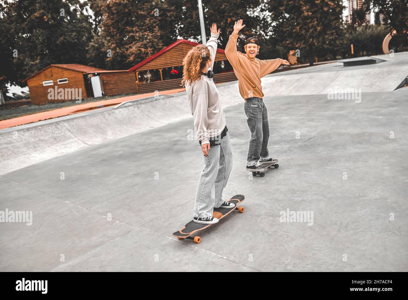Guy and girl sliding on skateboards with raised hand Stock Photo - Alamy