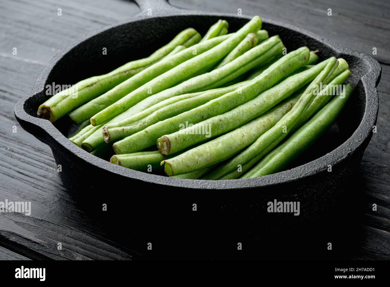 Fresh green French beans set, in frying cast iron pan, on black wooden ...